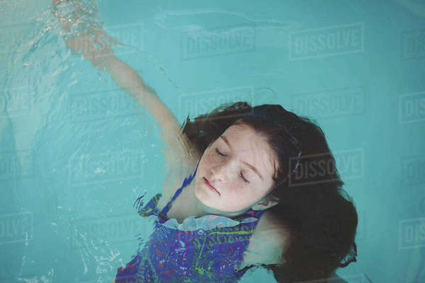 Caucasian girl floating in swimming pool - Stock Photo - Dissolve