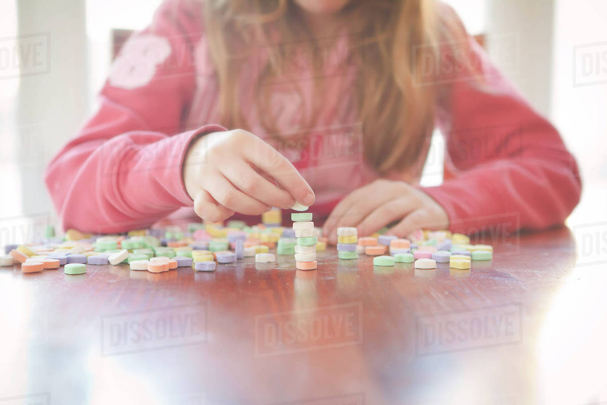 Caucasian girl stacking candy on table - Stock Photo - Dissolve