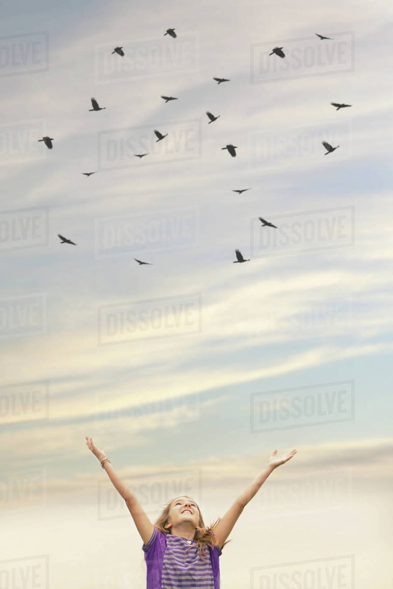 Caucasian girl cheering under flock of birds - Stock Photo - Dissolve
