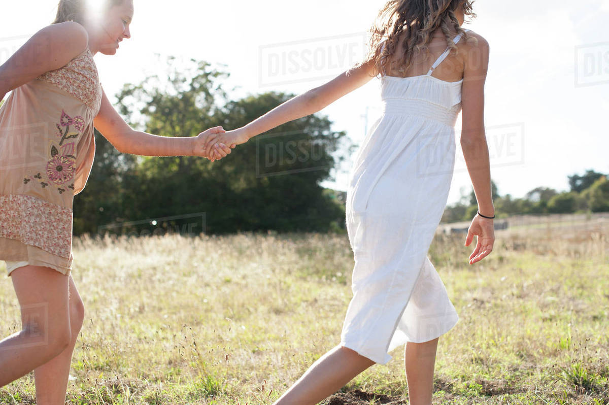 Girls holding hands in field - Stock Photo - Dissolve