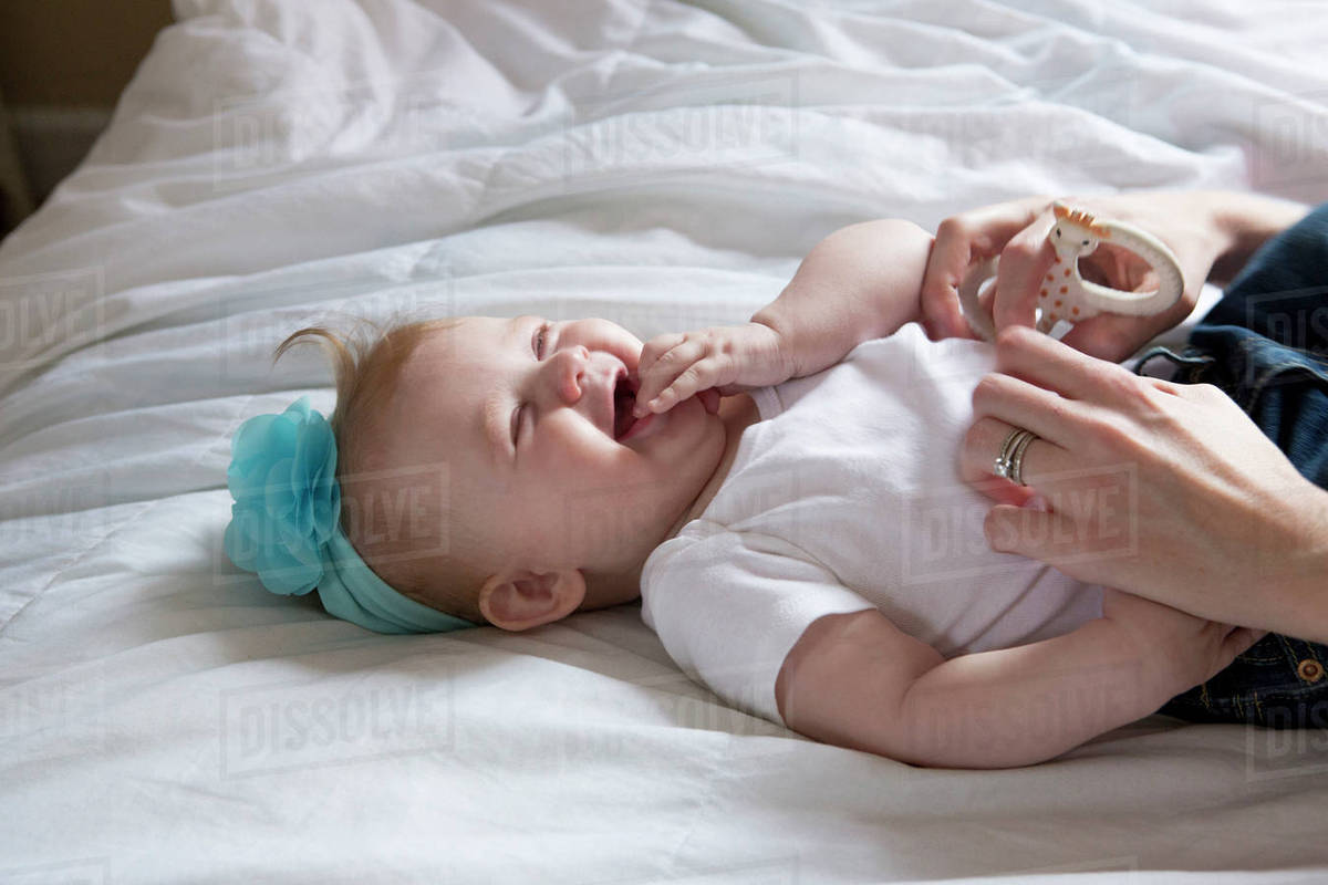Close up of mother tickling baby girl on bed - Stock Photo - Dissolve