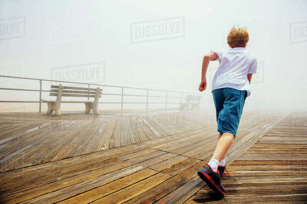 Caucasian boy running on wooden boardwalk - Stock Photo - Dissolve