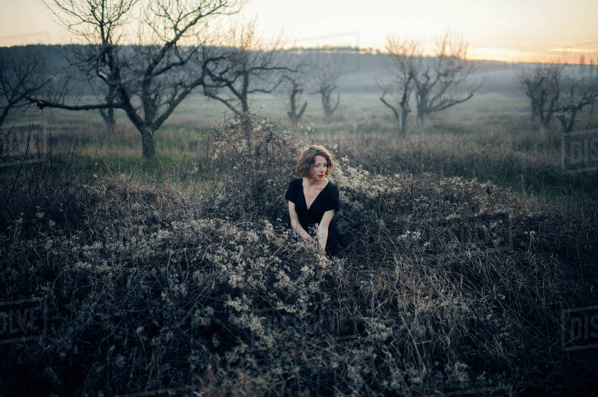Caucasian woman sitting in remote field - Stock Photo - Dissolve