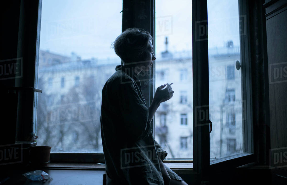 Caucasian woman smoking at open window - Stock Photo - Dissolve