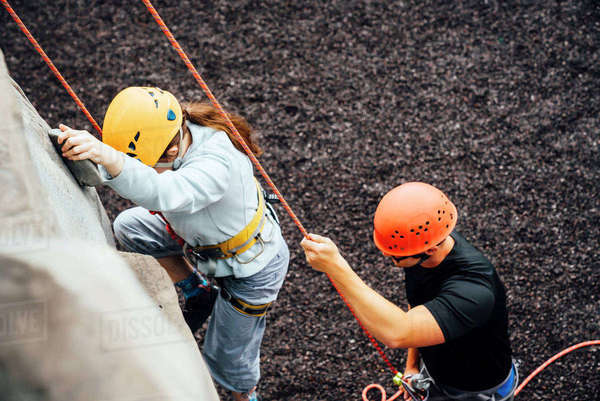 Caucasian man holding rope for woman climbing rock climbing wall ...