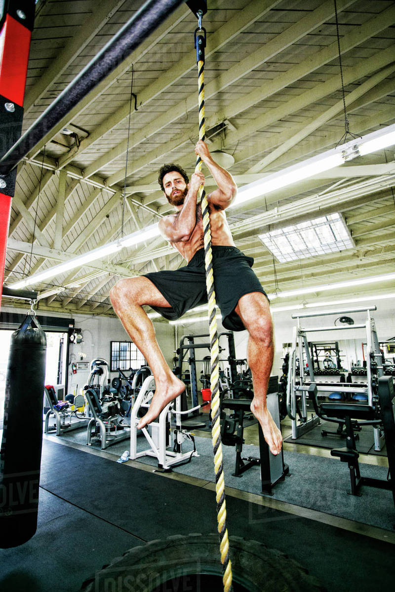Mixed Race man climbing rope in gymnasium - Stock Photo - Dissolve