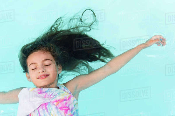 Smiling Caucasian girl floating in swimming pool - Stock Photo - Dissolve