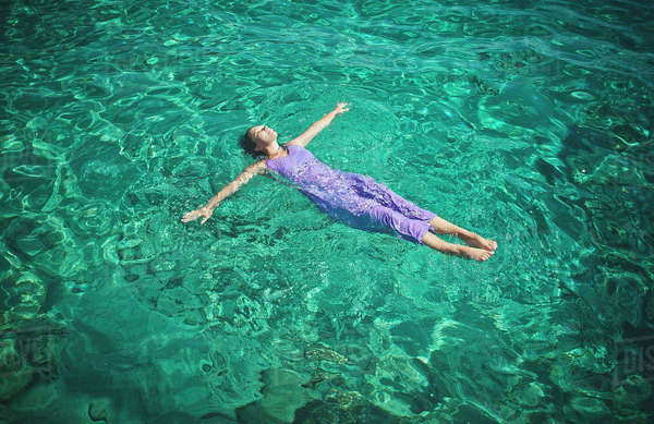 Caucasian woman wearing dress floating in water - Stock Photo - Dissolve