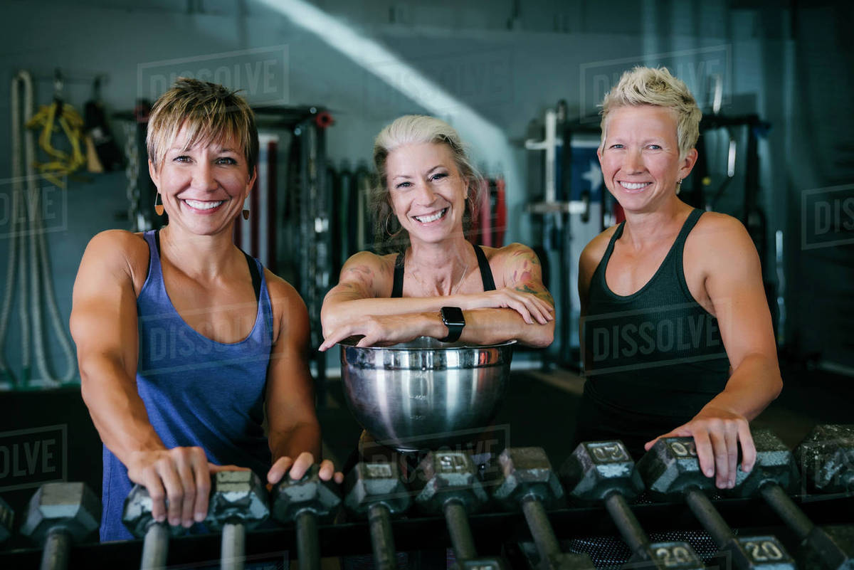 Smiling women leaning on rack in gymnasium - Stock Photo - Dissolve