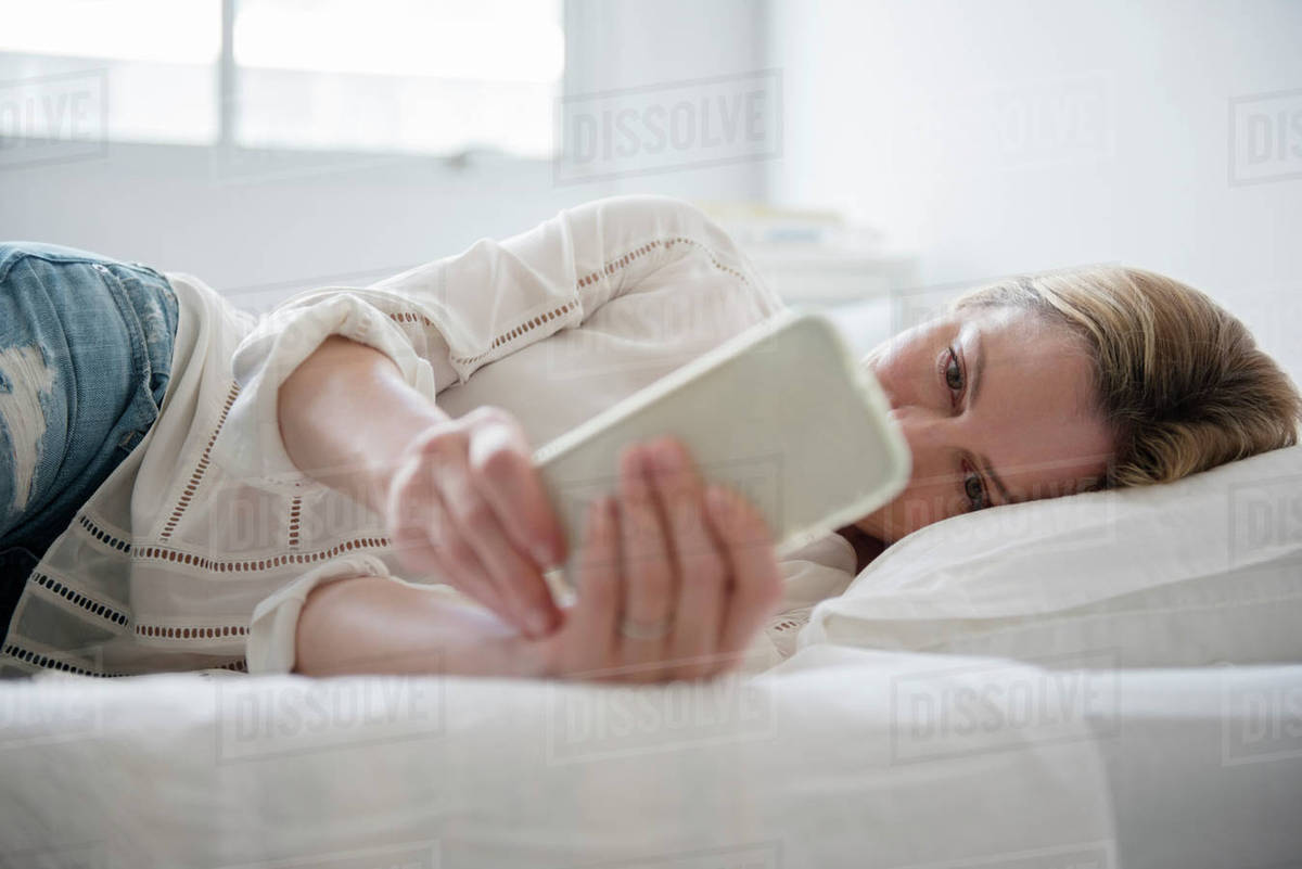 Woman laying on bed texting on cell phone - Royalty-free Stock Photo ...