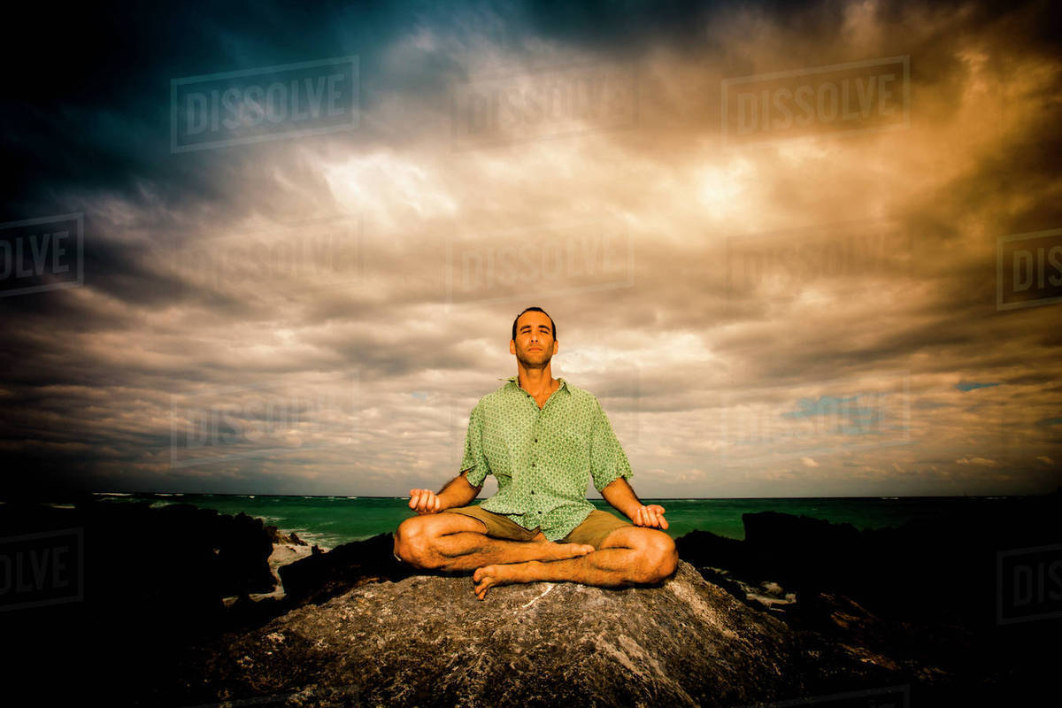 Man meditating on rock near ocean under clouds - Royalty-free Stock ...