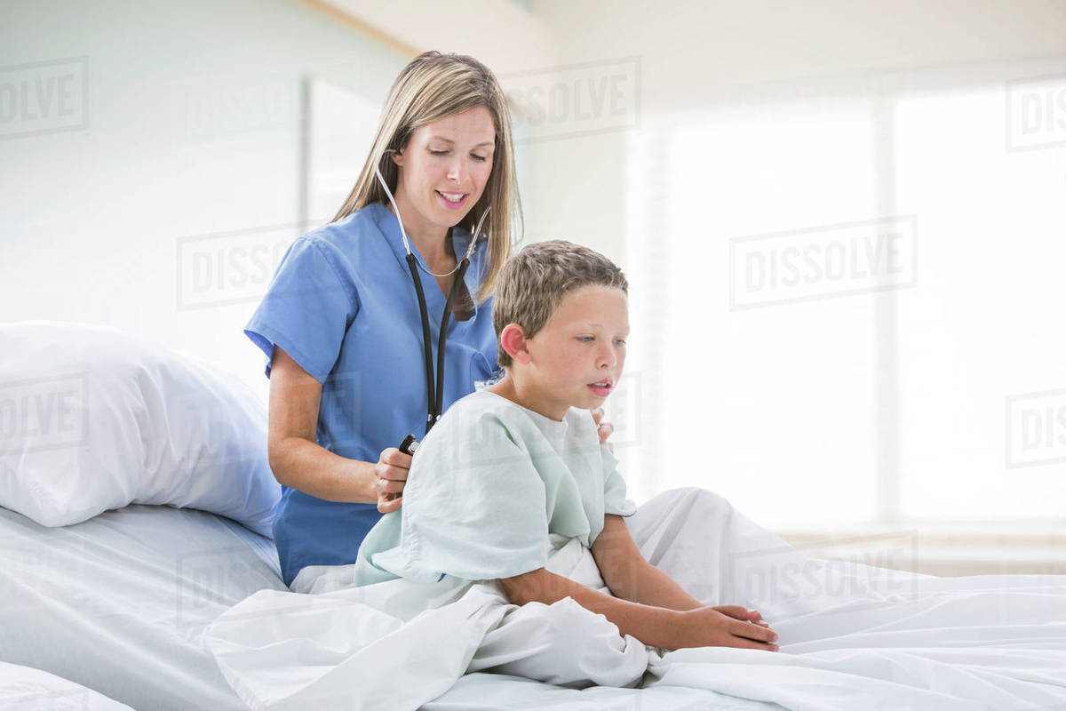 Caucasian nurse listening to chest of boy in hospital bed - Royalty ...