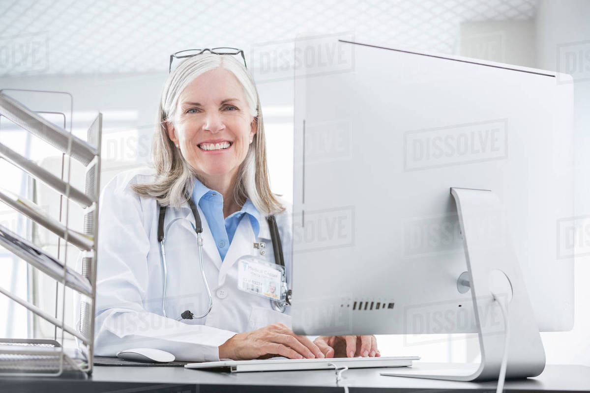 Smiling Caucasian doctor using computer at desk - Royalty-free Stock ...