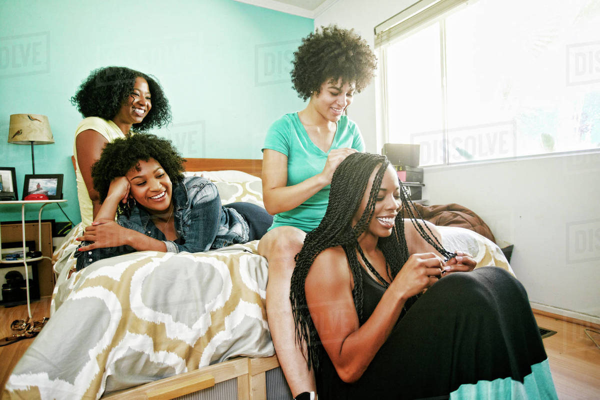 Woman braiding hair of friend in bedroom - Stock Photo - Dissolve