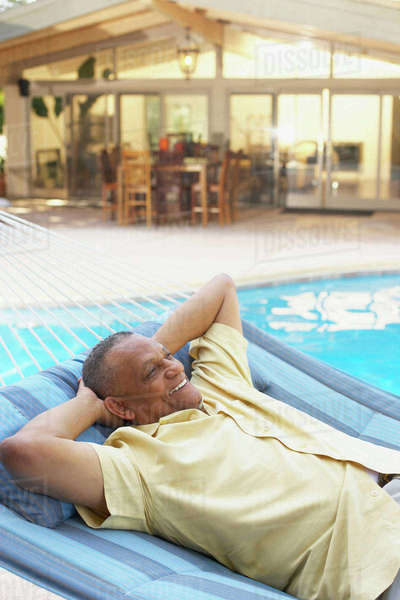 African man laying in hammock at poolside - Stock Photo - Dissolve