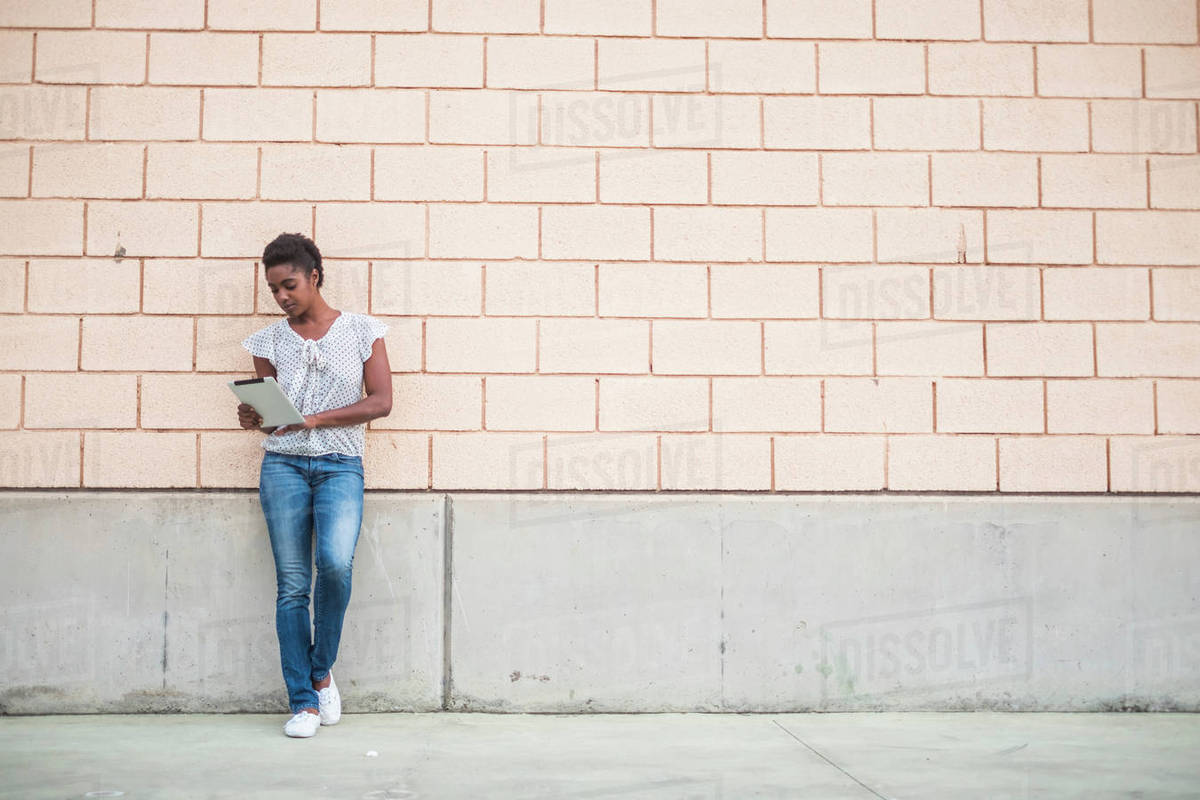 African American woman leaning on concrete wall using digital tablet ...