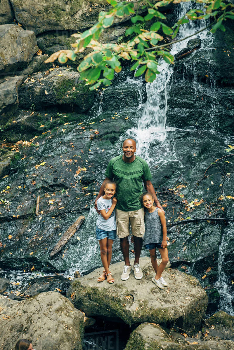 Father and daughters posing on rock near waterfall - Stock Photo - Dissolve