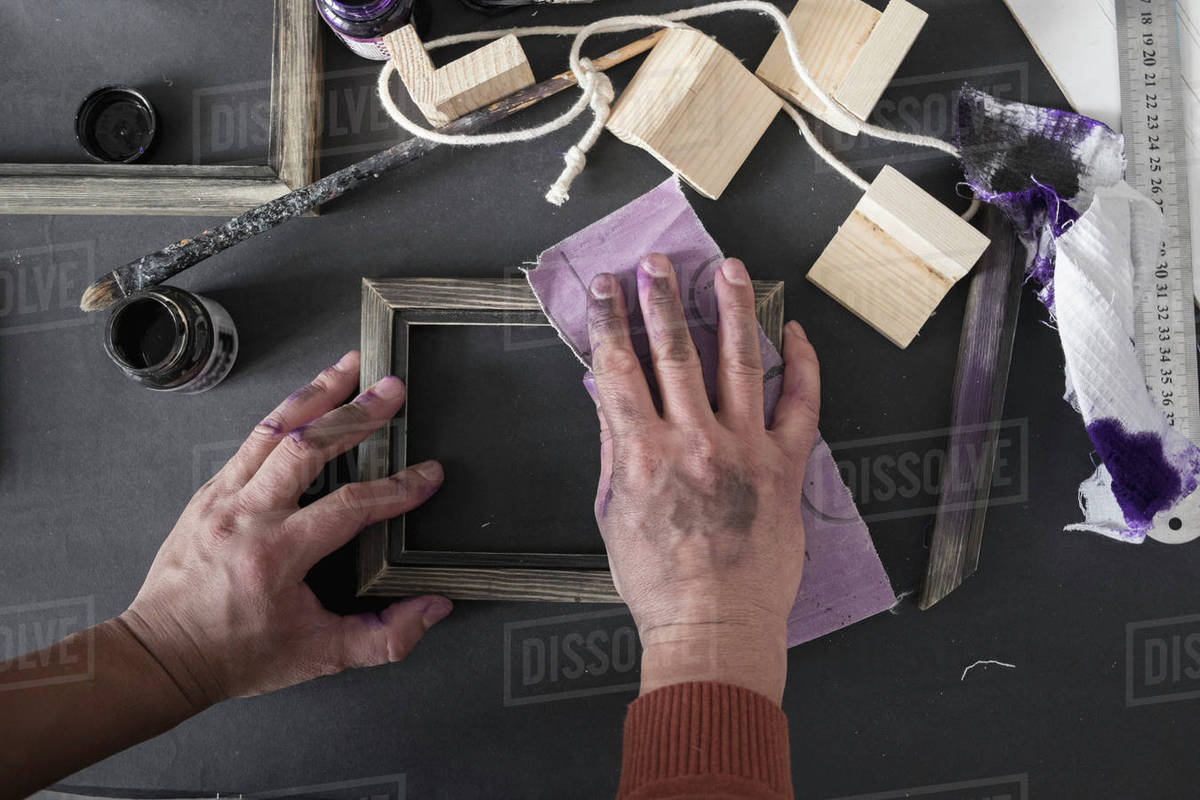 Hands of Caucasian artist sanding picture frame - Stock Photo - Dissolve