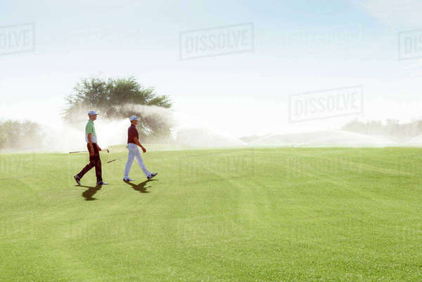 Friends walking on golf course near sprinklers - Stock Photo - Dissolve