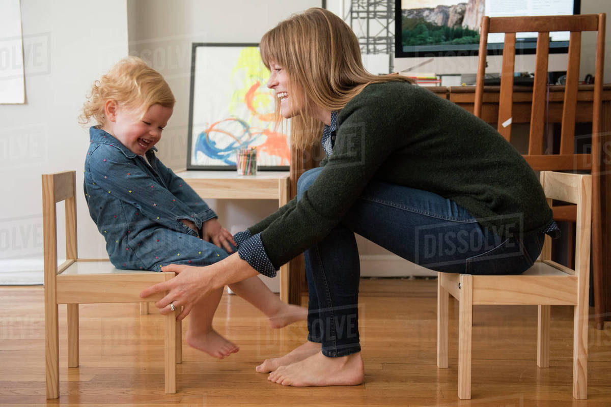 Caucasian mother and daughter sitting on small chairs in home office ...