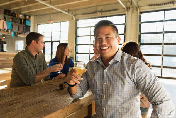 Portrait of smiling man drinking beer with friends in brew pub ...