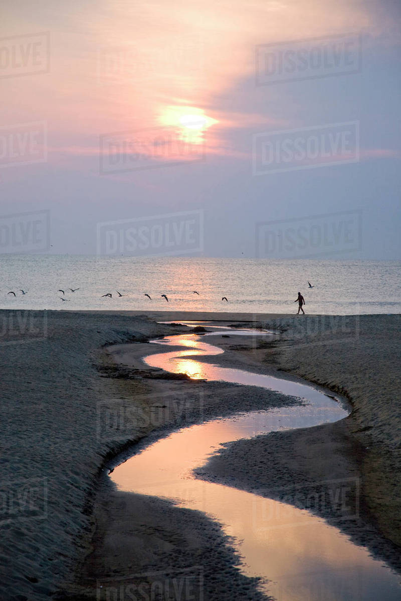 Man walking on beach near water channel at sunset - Royalty-free Stock ...