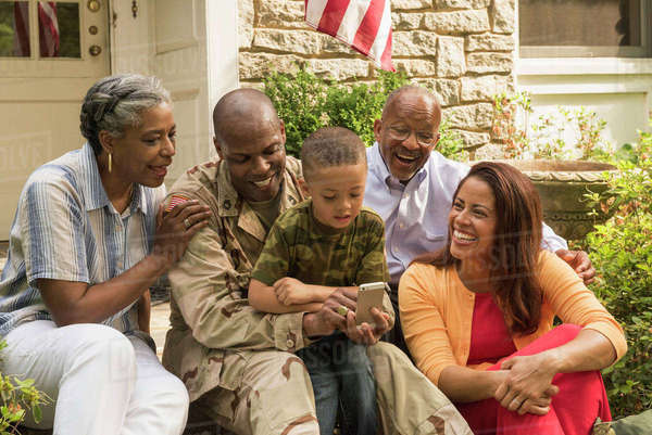 Soldier and multi-generation family looking down at cell phone ...