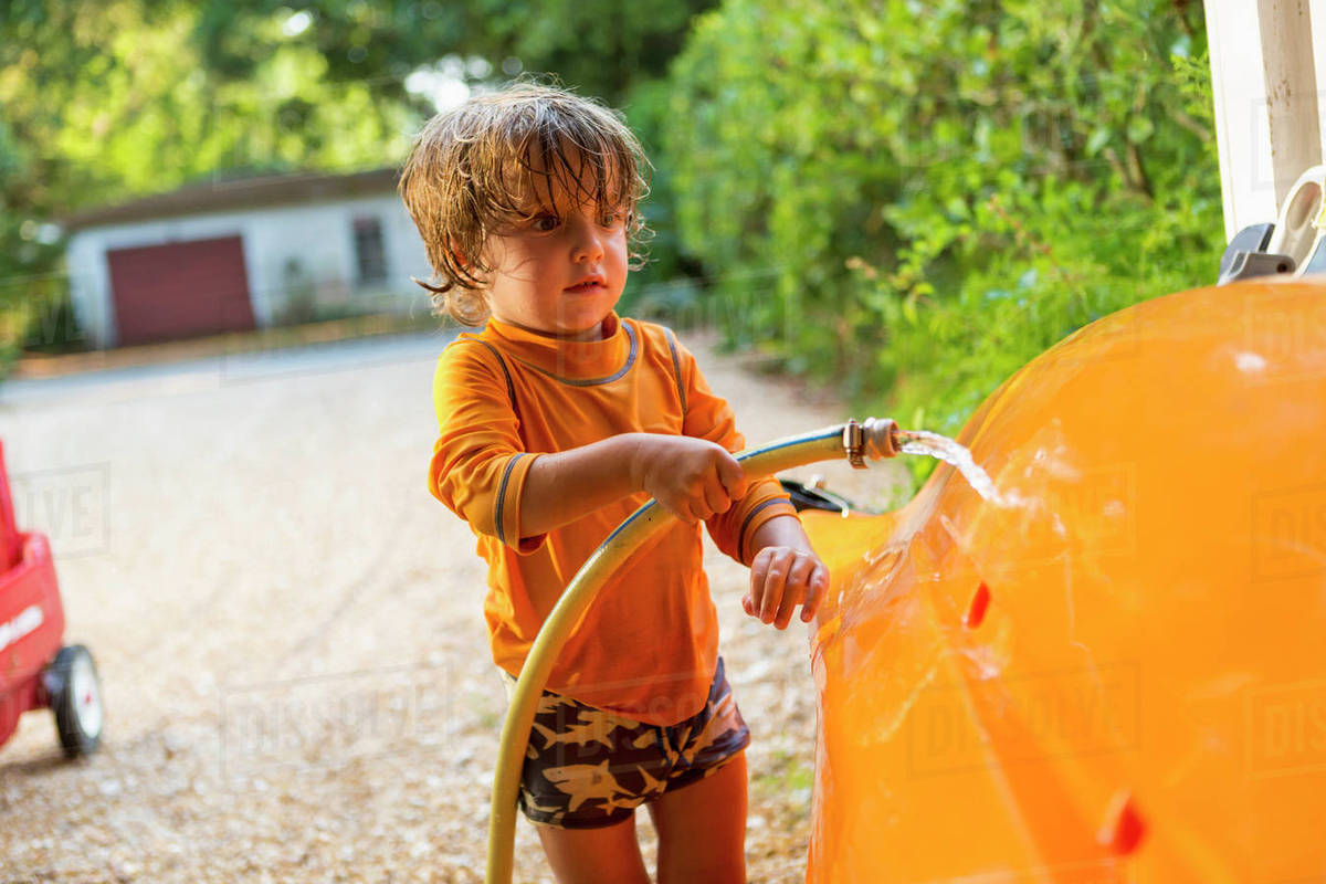 Caucasian boy washing kayak with hose - Royalty-free Stock Photo | Dissolve