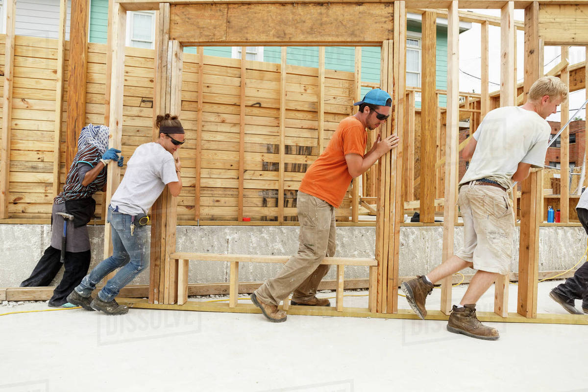 Volunteers pushing framed wall at construction site - Royalty-free ...