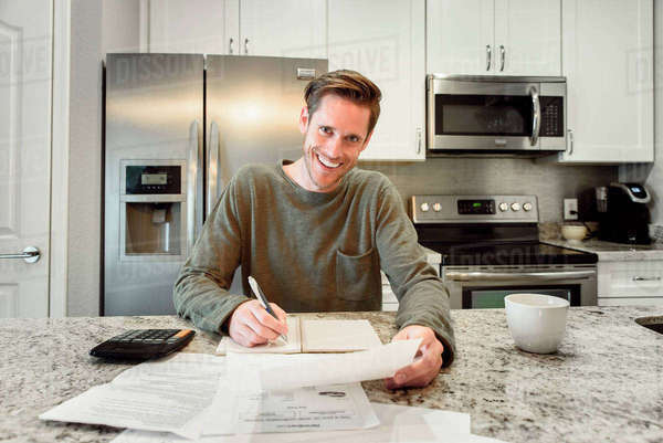 Smiling Caucasian man writing notes and reading paperwork - Stock Photo ...