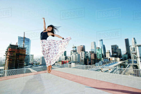 Asian woman jumping on urban rooftop - Royalty-free Stock Photo | Dissolve