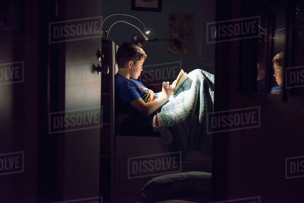 Caucasian boy reading book in bed at night - Royalty-free Stock Photo ...