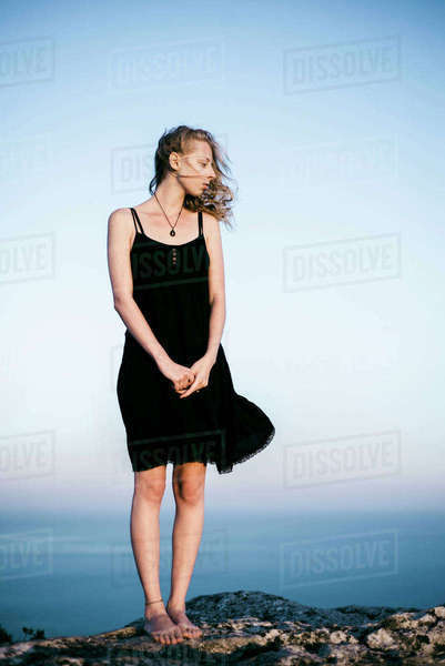 Wind blowing dress of Caucasian woman standing on rock near ocean ...