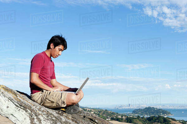 Climber using laptop on rocky hilltop - Royalty-free Stock Photo | Dissolve