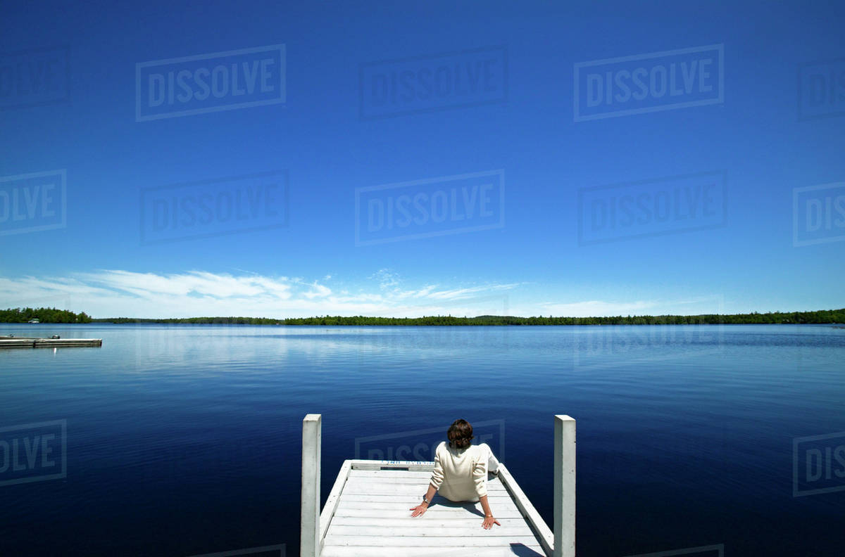 Woman overlooking lake on wooden dock - Royalty-free Stock Photo | Dissolve
