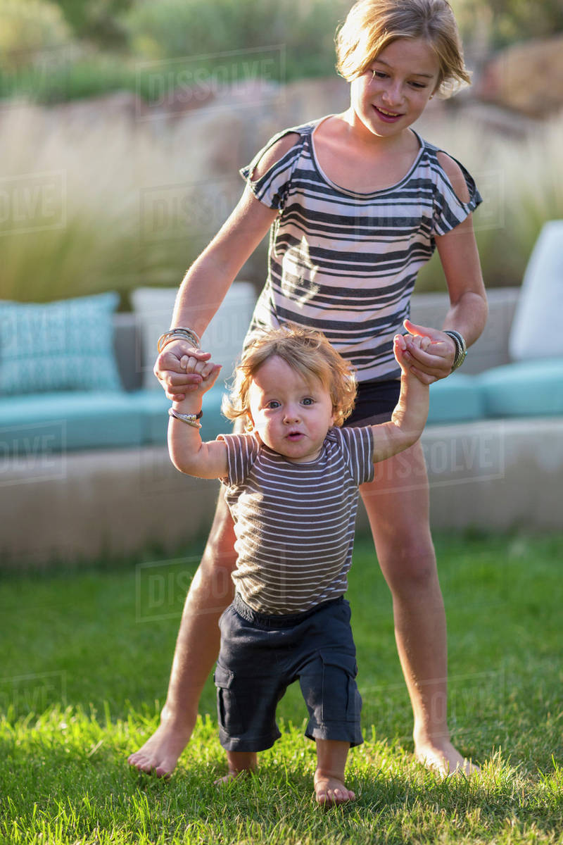 Caucasian sister helping baby brother walk in backyard - Royalty-free ...