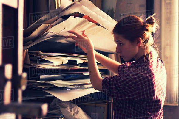 Caucasian artist sorting through papers in studio - Stock Photo - Dissolve