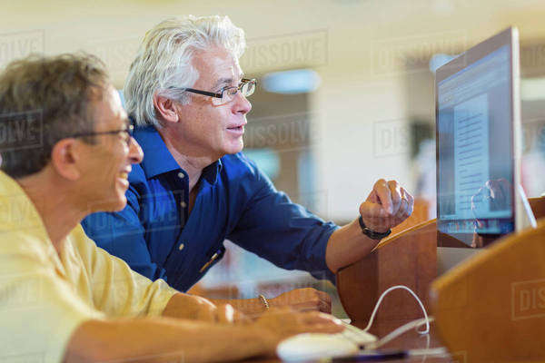 Teacher helping adult student use computer in library - Royalty-free ...