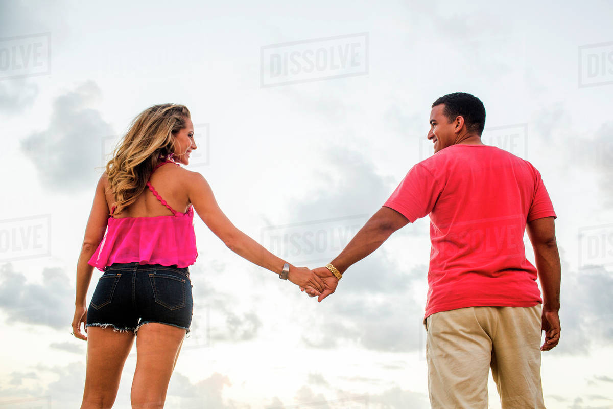 Low angle view of couple holding hands under cloudy sky - Royalty-free ...