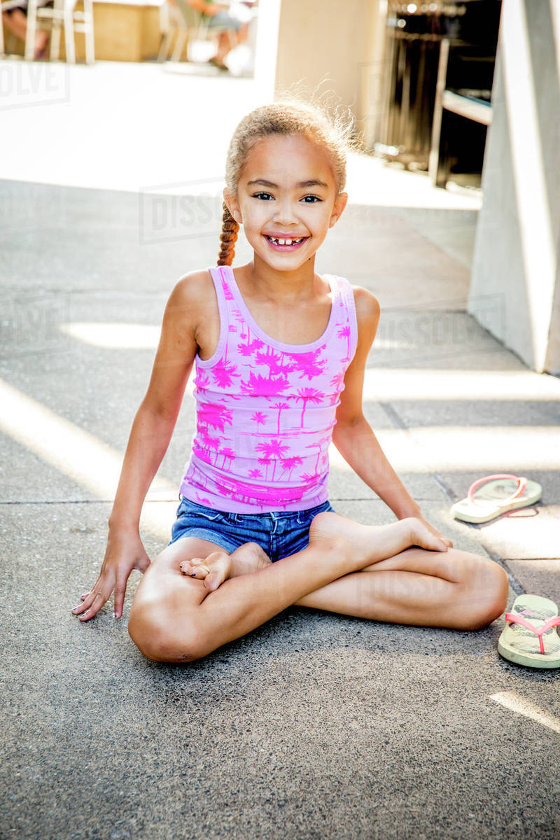Mixed race girl sitting with legs crossed on sidewalk - Stock Photo ...