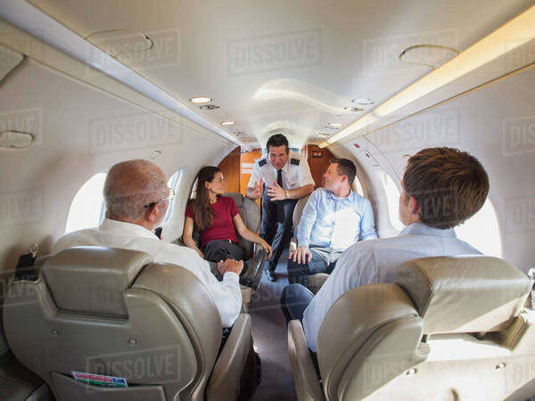 Pilot talking to business people on airplane - Stock Photo - Dissolve