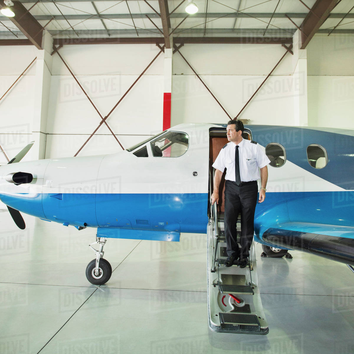 Caucasian pilot disembarking airplane in hangar - Royalty-free Stock ...