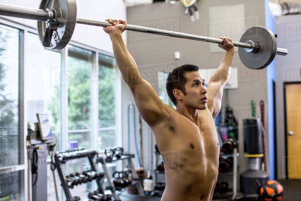 Pacific Islander man lifting weights in gym - Stock Photo - Dissolve