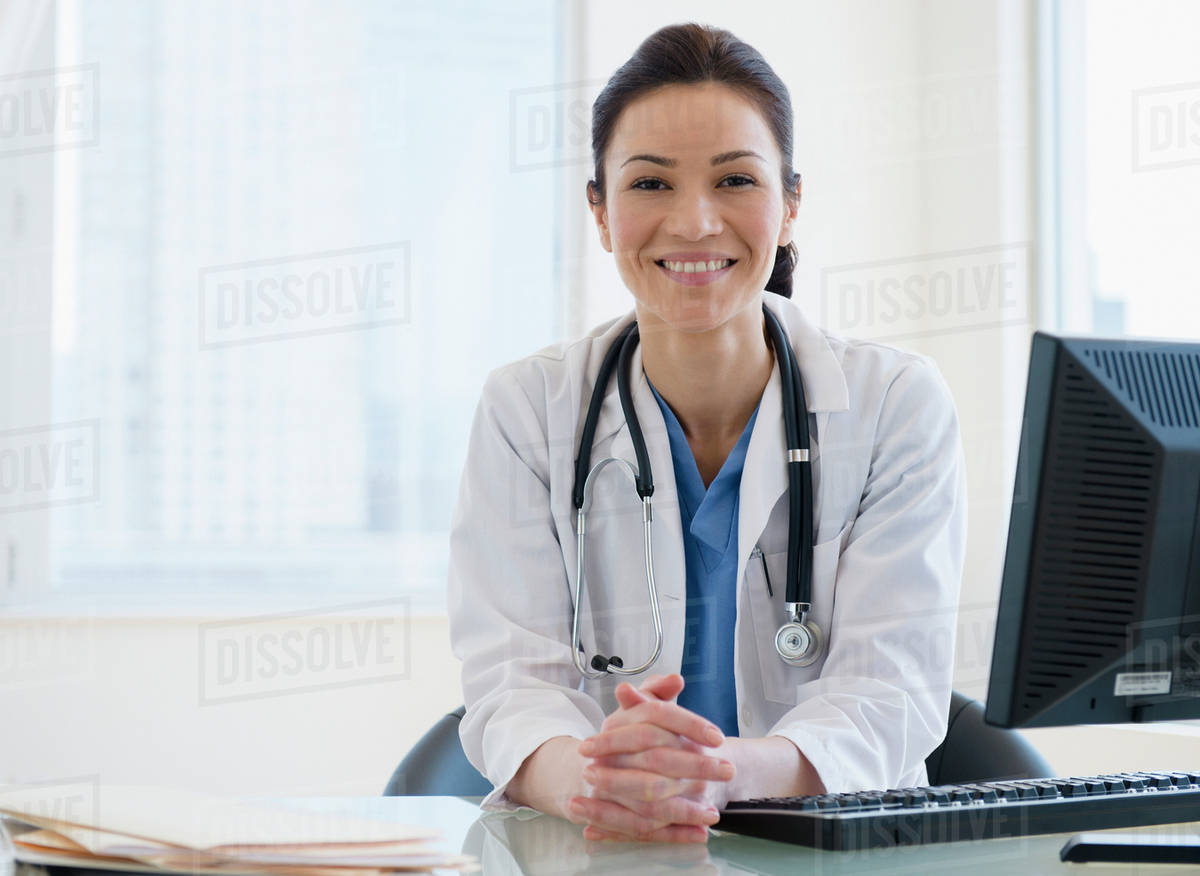 Caucasian doctor smiling at desk - Royalty-free Stock Photo | Dissolve
