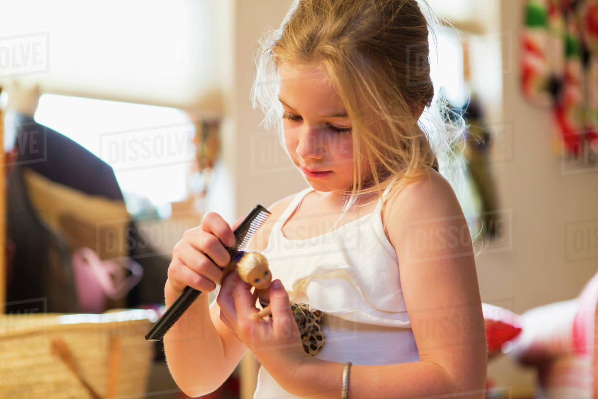 Caucasian girl combing doll's hair - Stock Photo - Dissolve