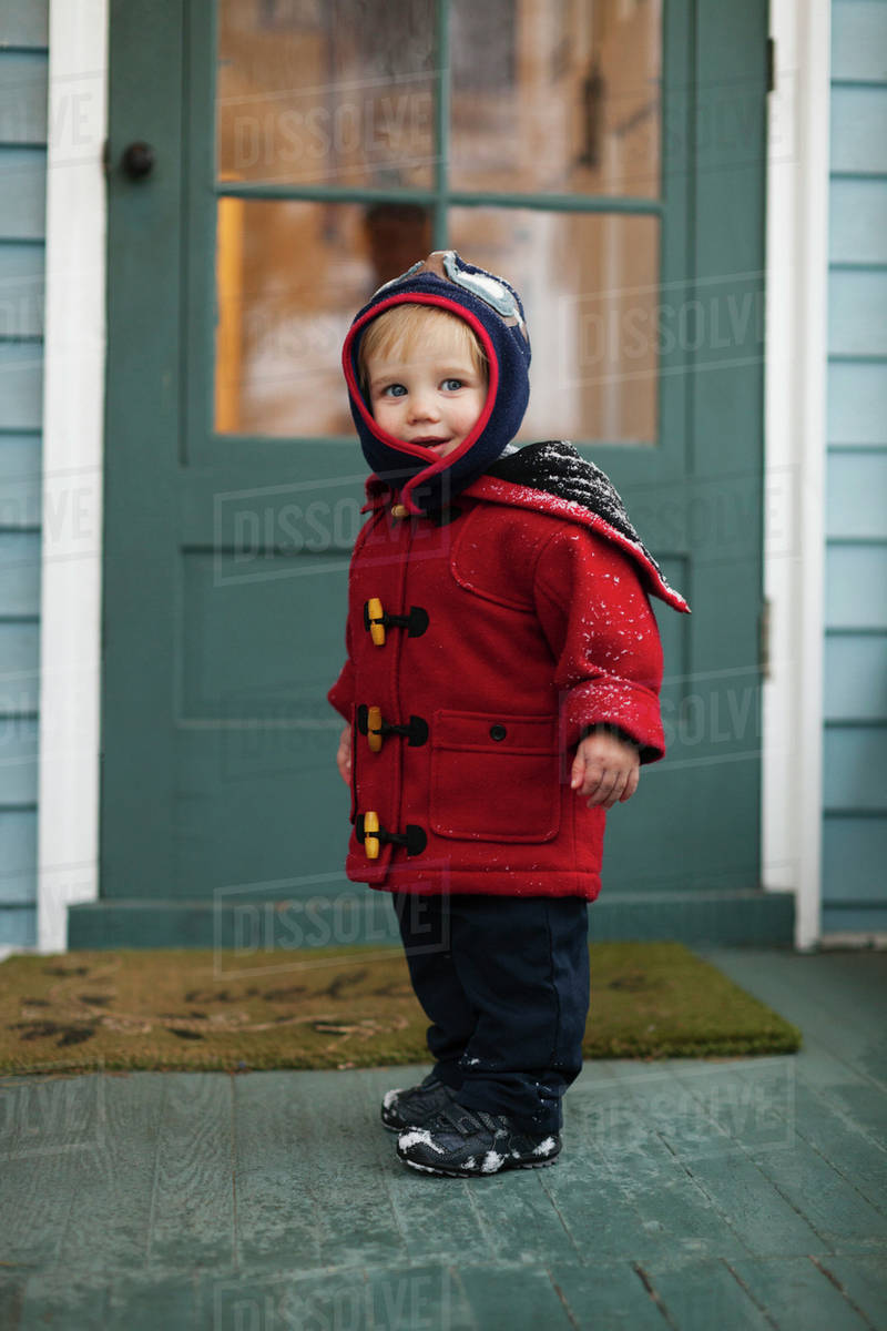 Caucasian boy wearing winter coat on porch - Stock Photo - Dissolve