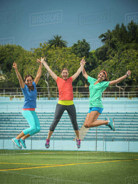 Caucasian women jumping for joy in stadium field - Stock Photo - Dissolve