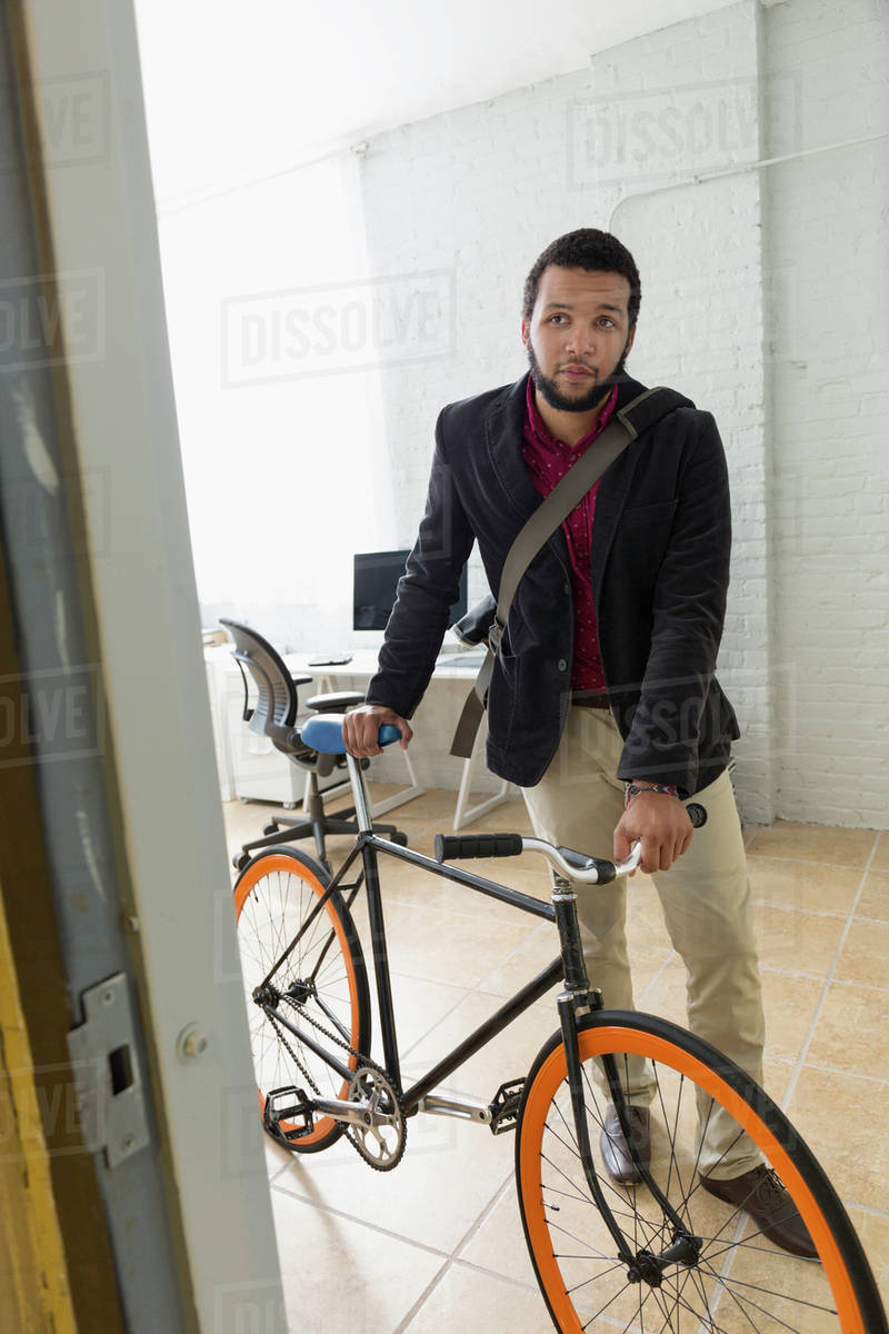 Mixed race businessman wheeling bicycle in office - Stock Photo - Dissolve