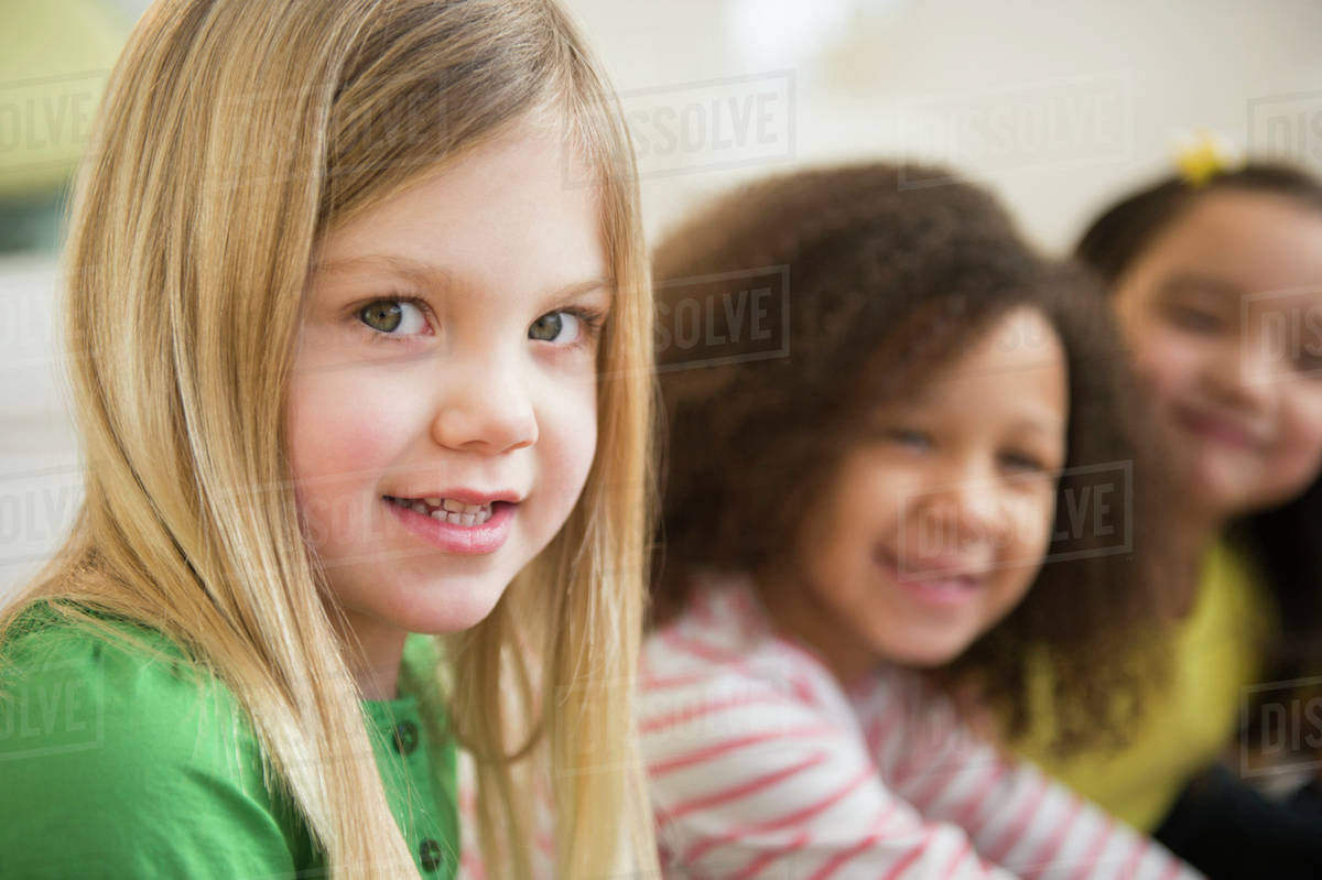 Smiling girls sitting in line - Stock Photo - Dissolve