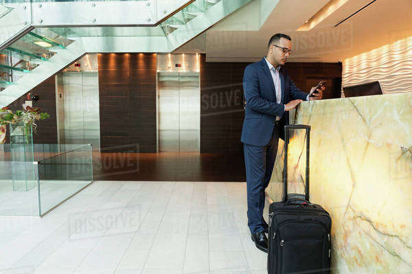 Hispanic businessman using cell phone at hotel front desk - Royalty ...